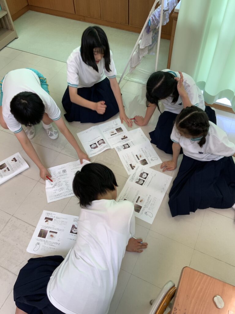 ちょっといい感じだと思いませんか。床に座り込んで、頭を突き合わせて考え込んでいるのは理科のプリント。知恵を合わせて、ああでも無い、こうでも無い。「難しい！」って。